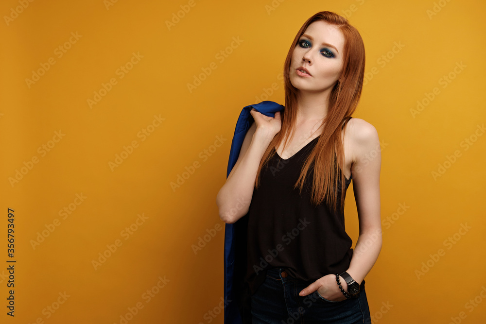 girl in a black top and blue smokey stands on a yellow background ...