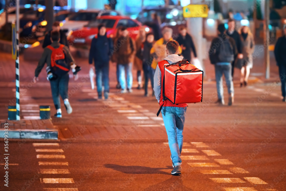 Deliveryman walking with red thermal bag on the night city street ...