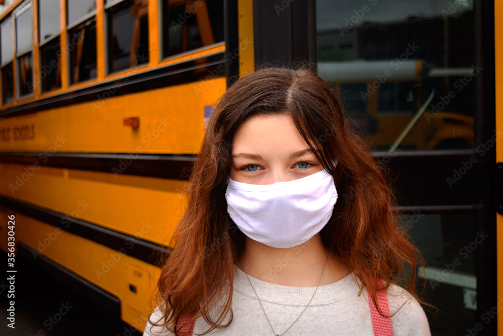 Child wearing face mask by school bus. A girl with a facemask stands by ...