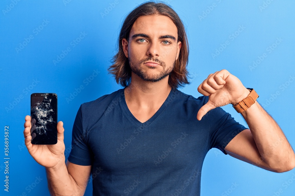 Young handsome man holding broken smartphone showing cracked screen ...