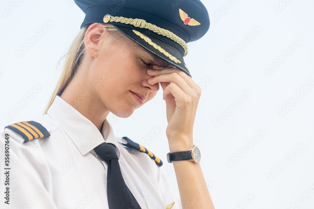 Sleepless tired young female pilot in uniform with her hand on her face ...