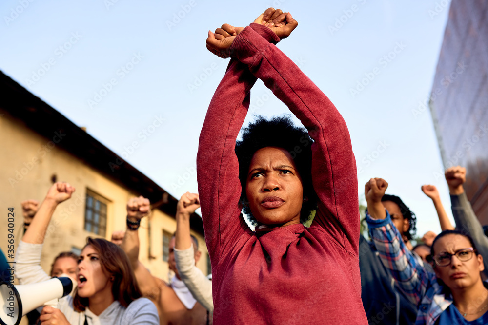 Black woman with clenched fists above her head protesting with group of ...