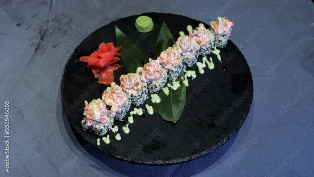 Appetizing sushi maki rotates on the black plate above grey background ...