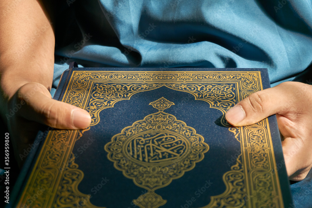 Close up of hand holding Holy Al Quran with written arabic calligraphy ...