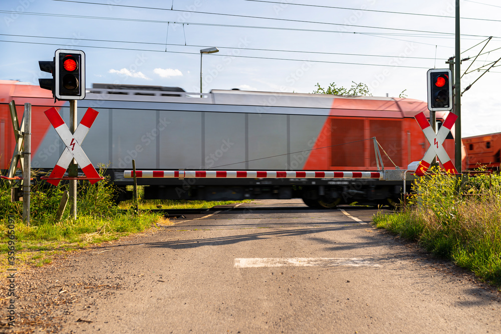 Closed barrier at a railway crossing with red warning lights on, a ...