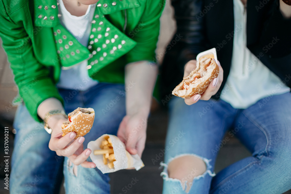 Funny girls sitting at street and eating fast food, having dinner ...