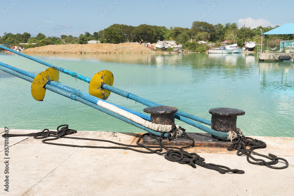 Mooring cables with rat guards are tied to a bollard to secure a large ...