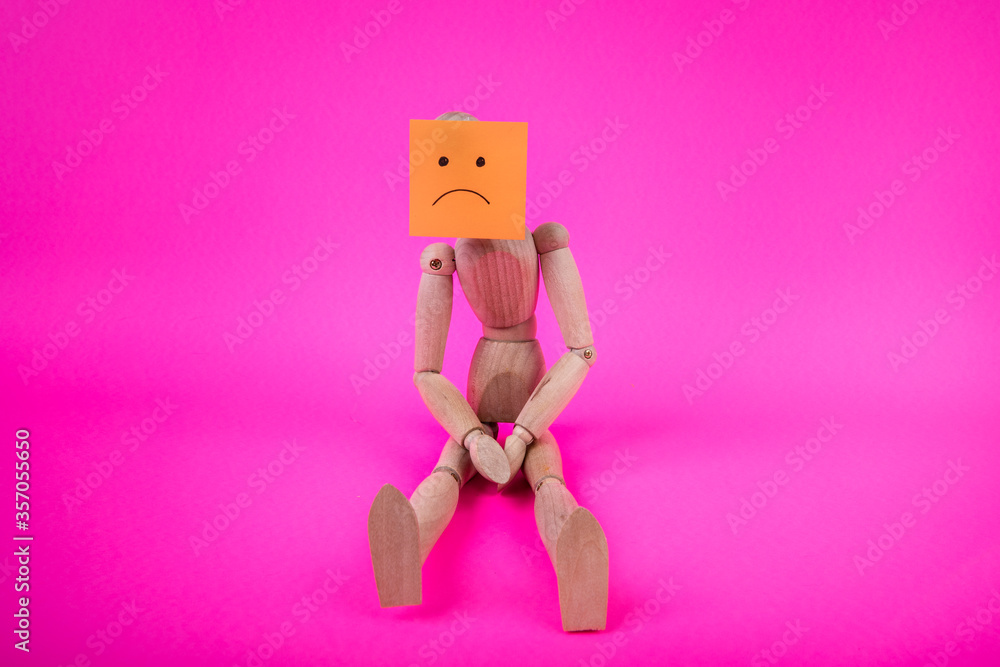 Wooden jointed doll sitting hunched over depressed with a sad face sign ...