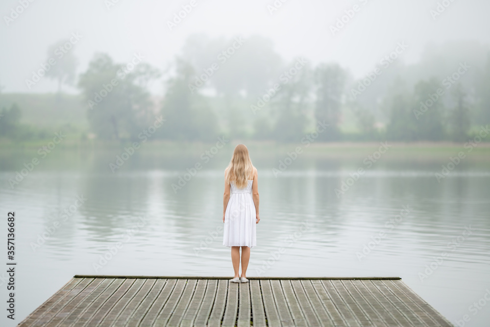 One young woman in white dress standing on edge of footbridge and ...
