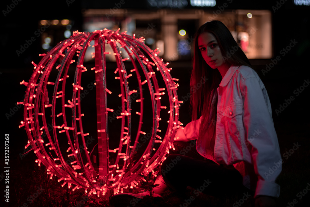 The girl at night sits near a glowing ball of red color. A glowing ball ...