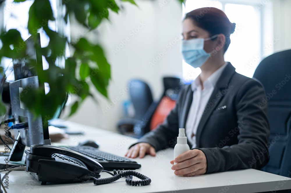 Female office manager in a mask at the desk using an antiseptic to ...