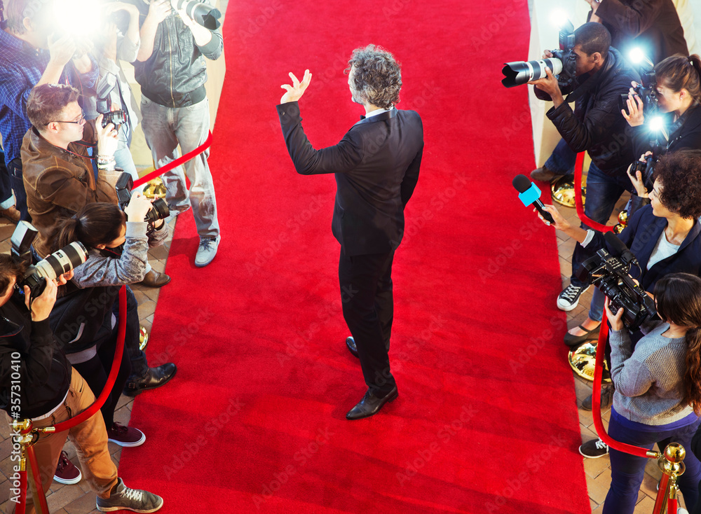 Celebrity arriving at red carpet event waving at photographing ...
