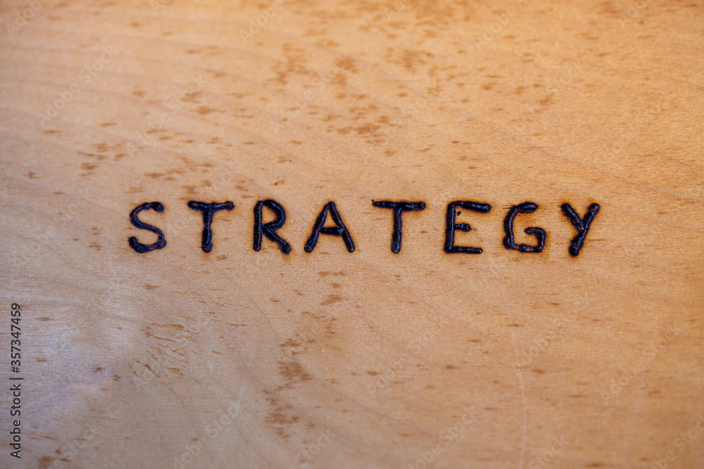 the word strategy handwritten on flat bare plywood surface with ...