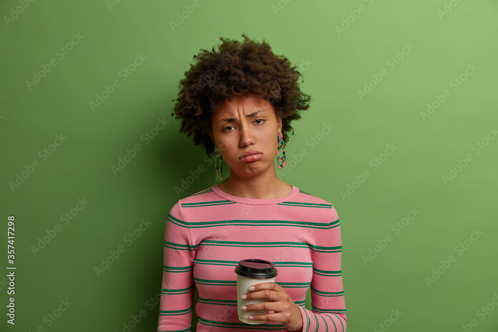 Photo of displeased gloomy curly woman feels tired and exhausted, holds ...