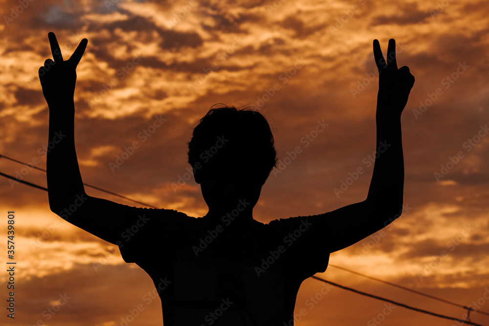 Silhouette of a kid raising his arms and doing peace sign with his hand ...