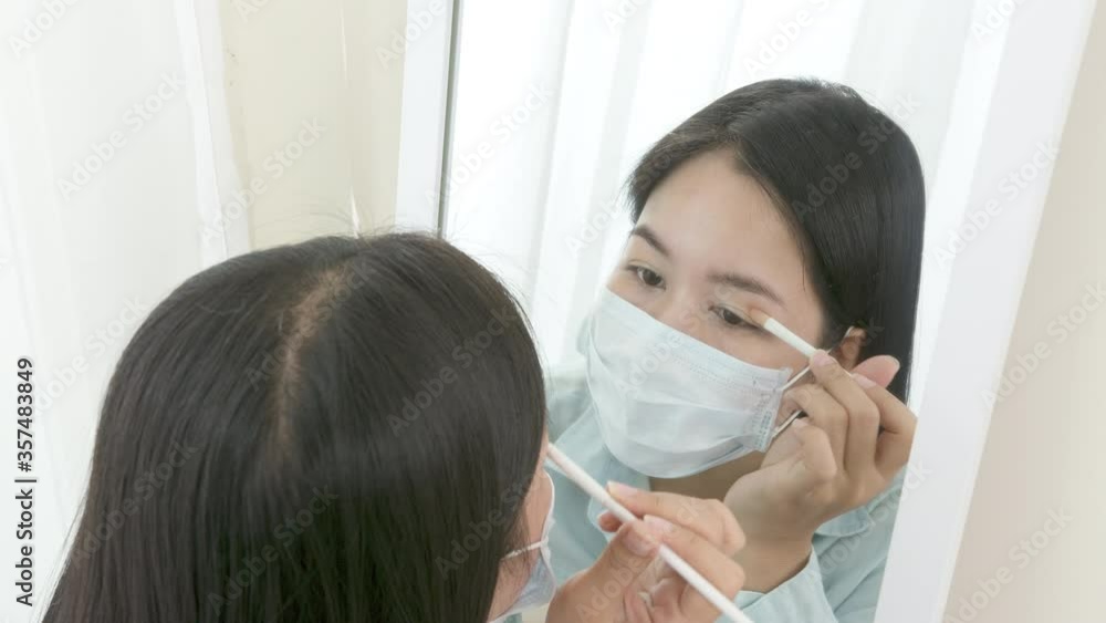 Mirror reflection asian woman wear surgical face mask apply cosmetic make up for go out to work ...