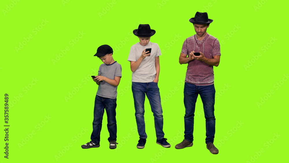 Father with two sons standing and using smart phones on green screen ...