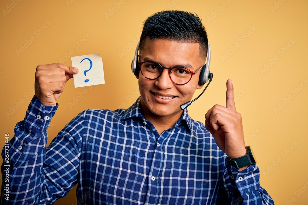 Young latin call center agent man holding question mark reminder paper ...
