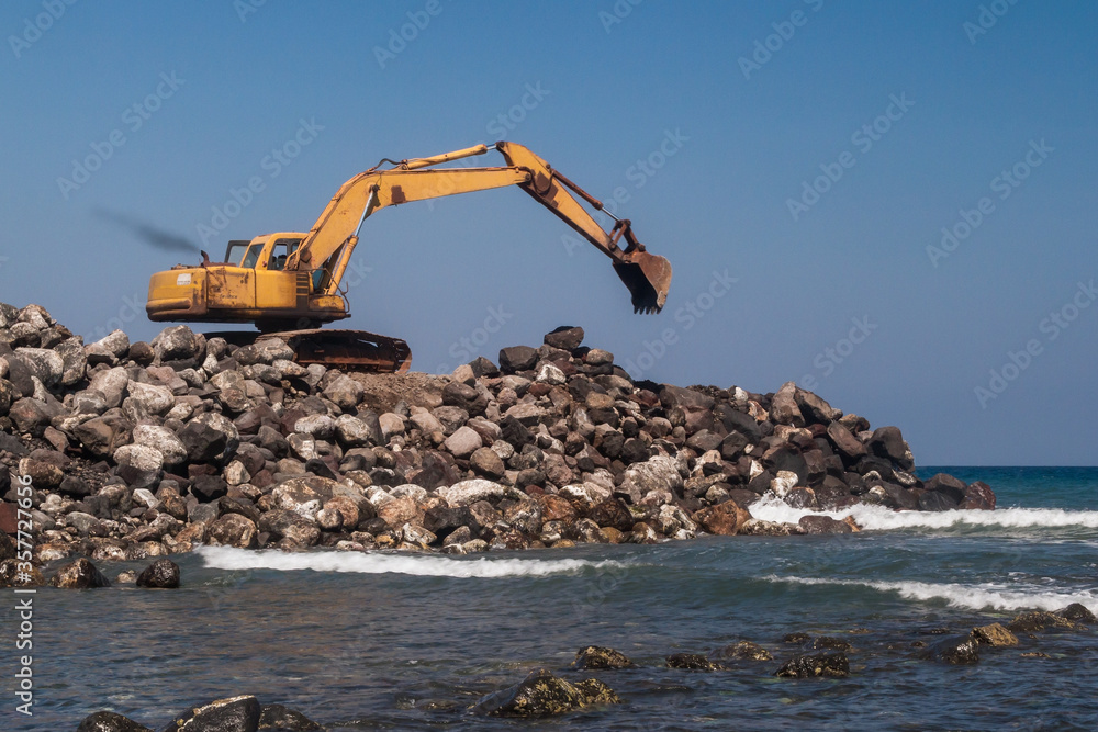 Excavator digger stone working on construction site on beach sea ocean ...
