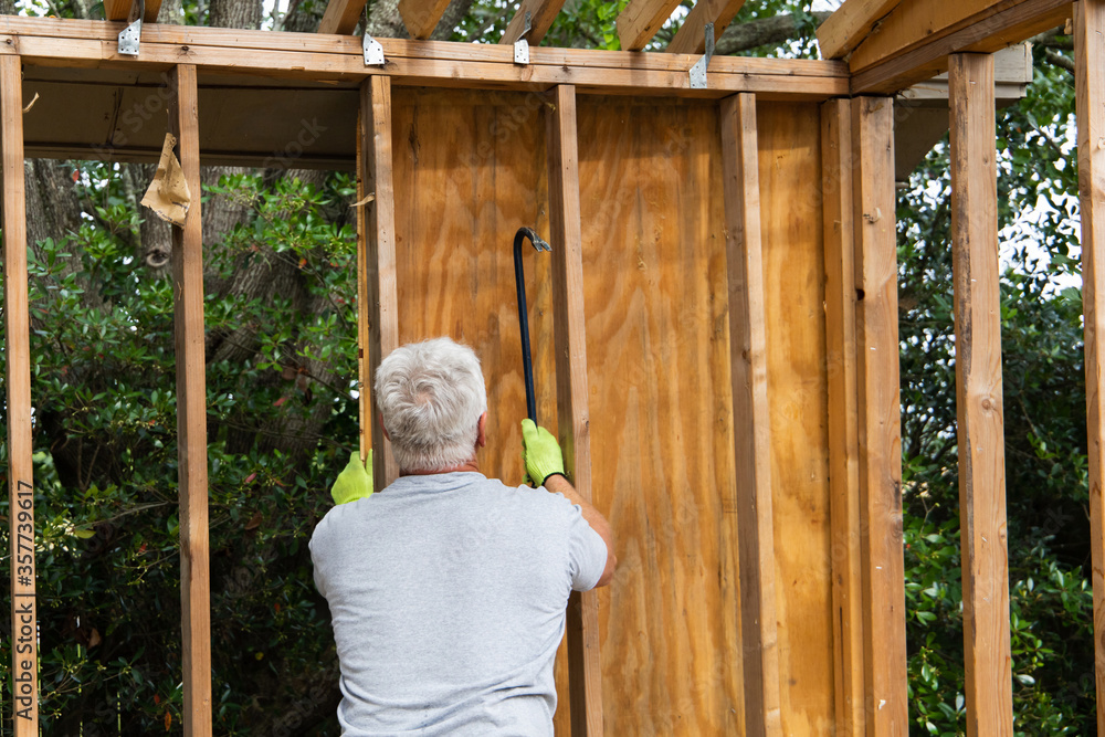 Demolition phase with a man tearing down an old shed with a crowbar in ...