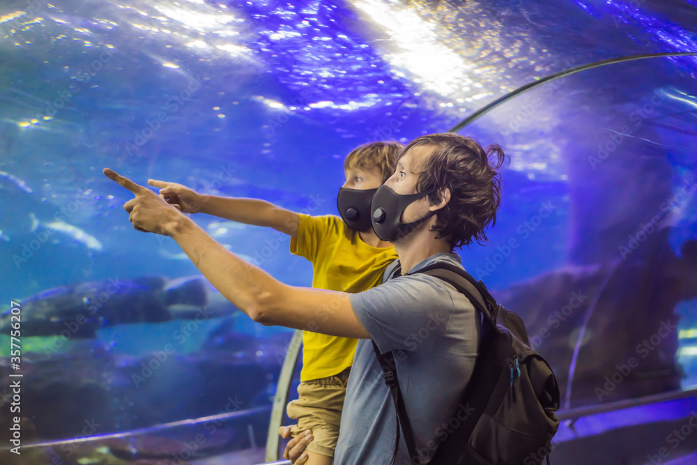 Dad and son in medical masks look at the fish in the aquarium in ...