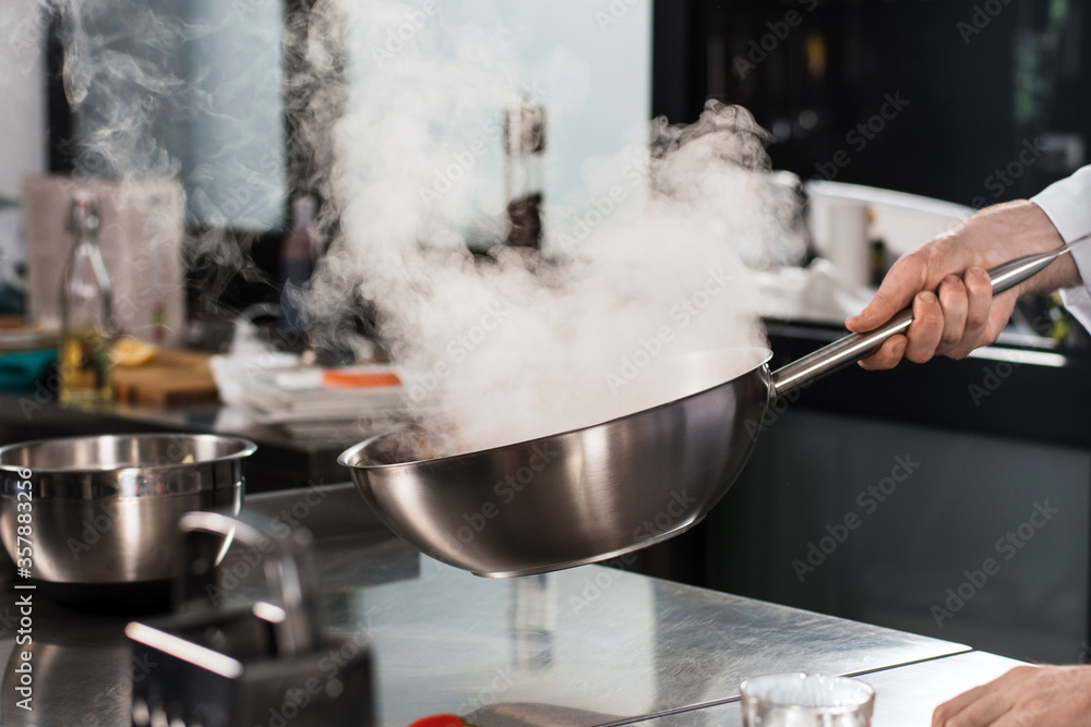 Chef hands keep wok at professional kitchen. Closeup chef hands cook ...