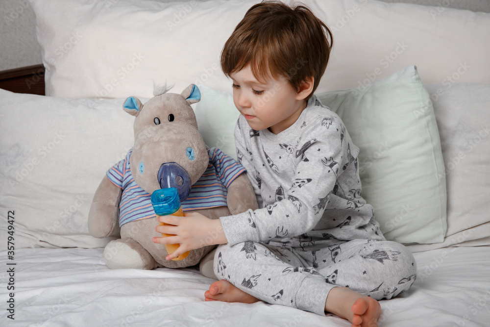 beautiful boy is sitting with a toy on the bed in an inhalation mask ...