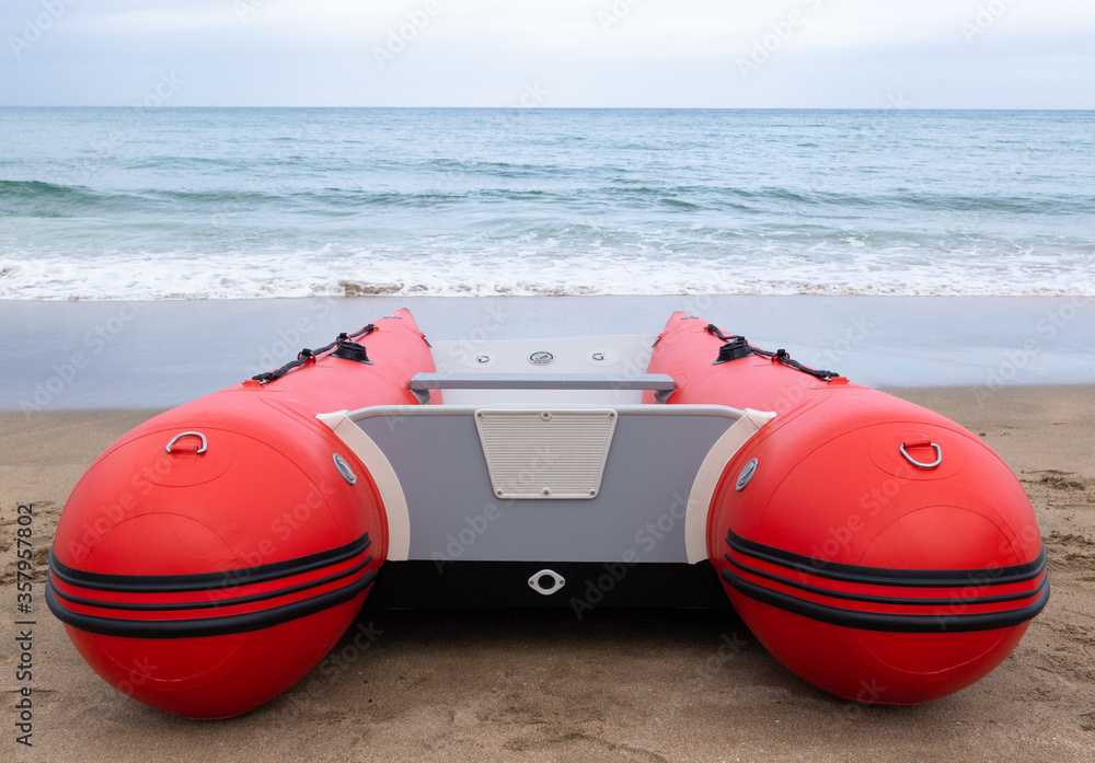 An inflatable boat on the beach it is red in color with a grey floor ...