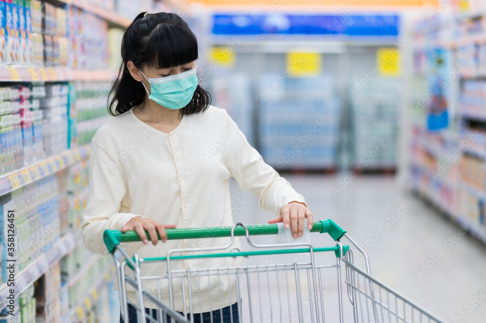Asian woman wearing medical face mask wipes shopping cart handle in ...