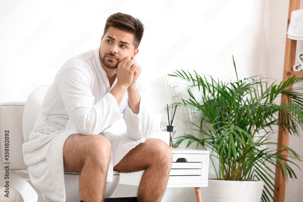 Young man sitting on toilet bowl in restroom Stock Photo | Adobe Stock