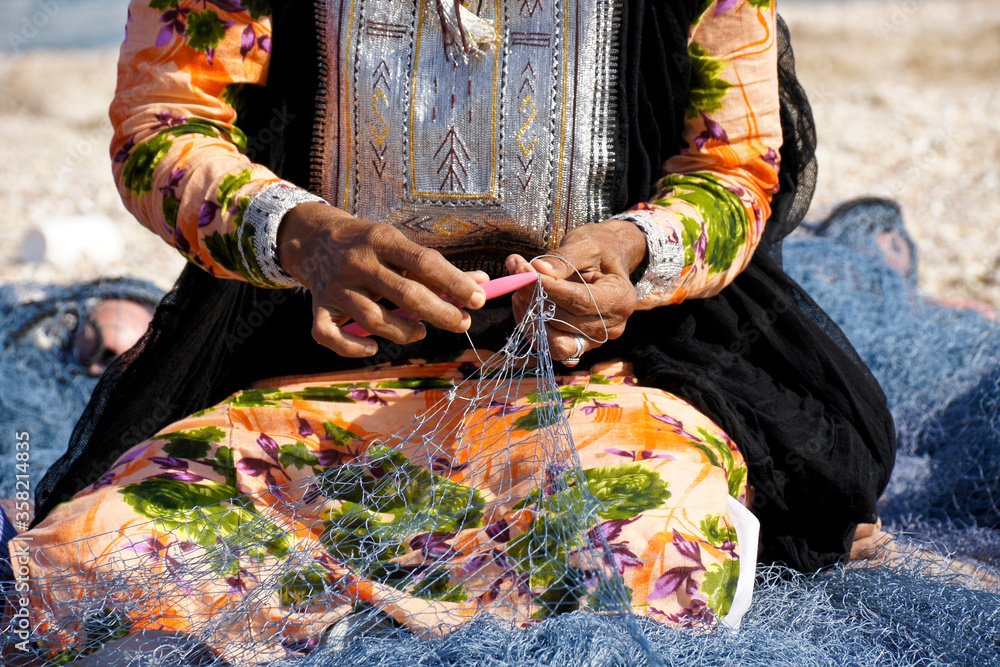 Photo & Art Print Omani woman in traditional dress mending fishing net ...