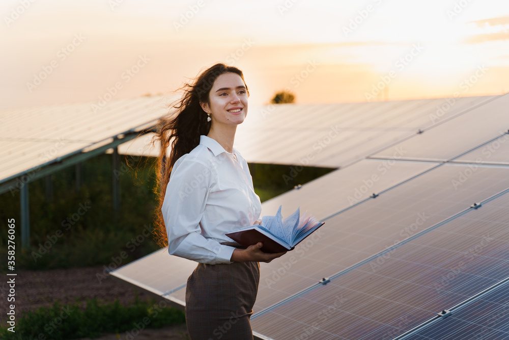 Girl and solar panels stands in row on the ground at sunset. Woman ...