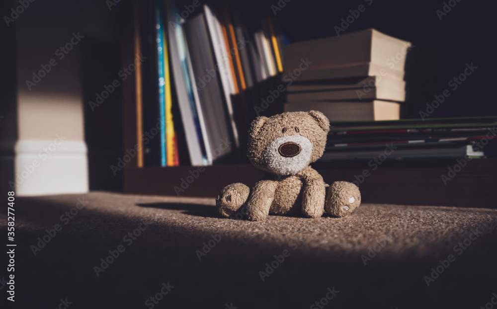 Teddy bear is sitting on carpet next to blurry bookshelf background ...