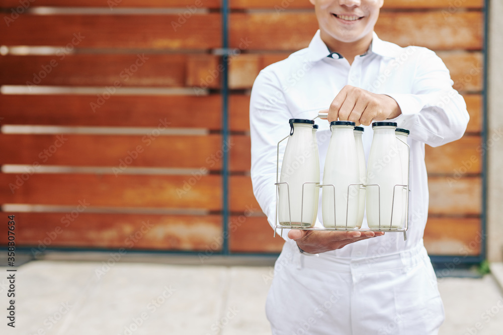 Young milkman in perfect white uniform standing against wooden fence ...