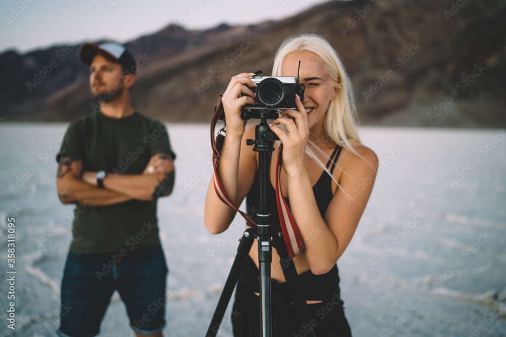 Skilled blonde female holding camera with modern objective taking photo ...