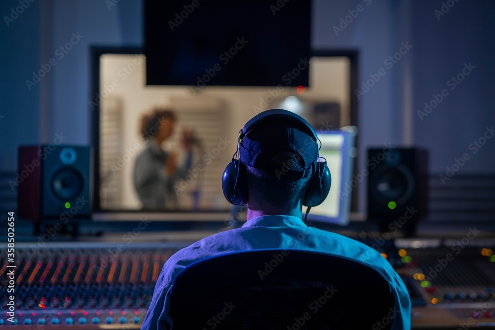 Back view of professional male sound producer with headphones is ...