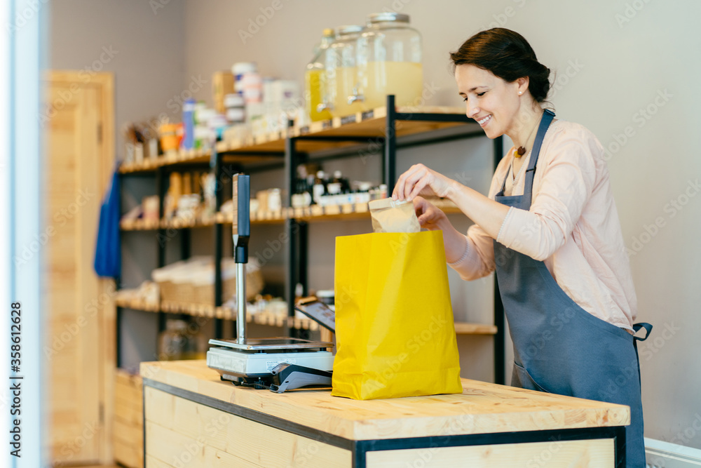 Smiling shopkeeper in package free grocery store collects paper bag of ...