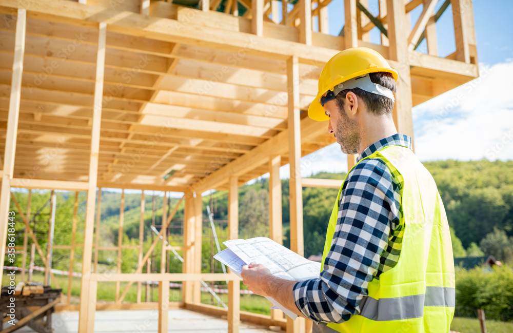 Engineer with hardhat and blueprints on building site of wood frame ...