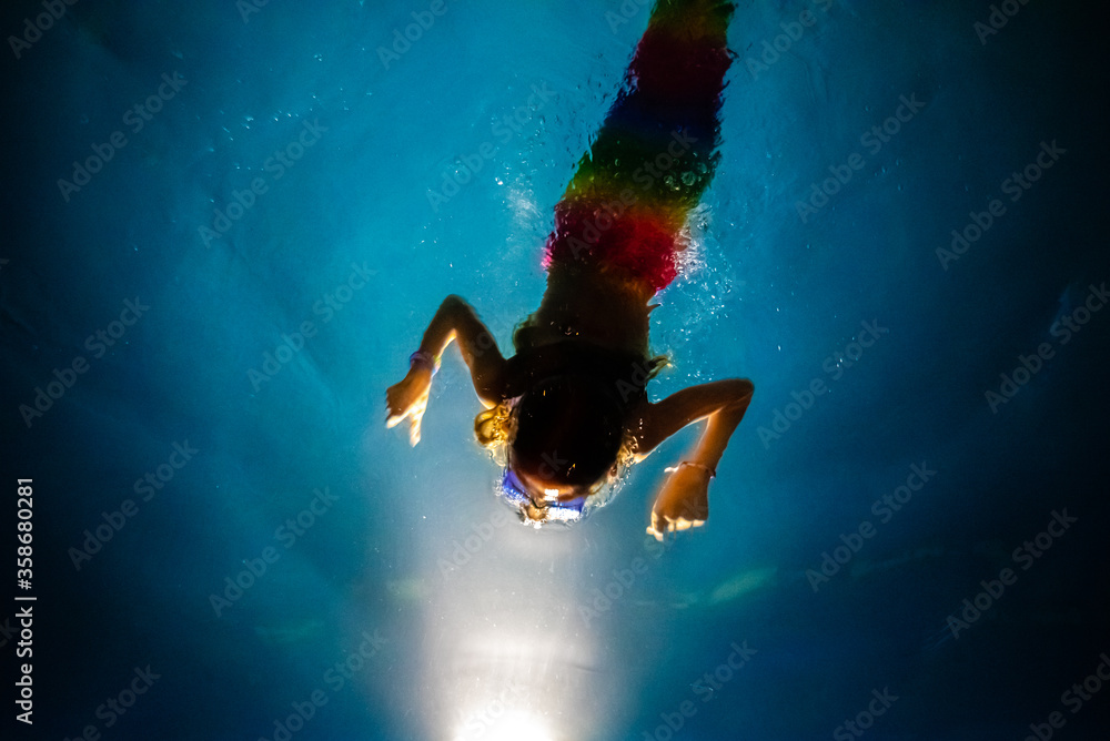 Girl disguised as a mermaid diving towards the light of a blue pool ...