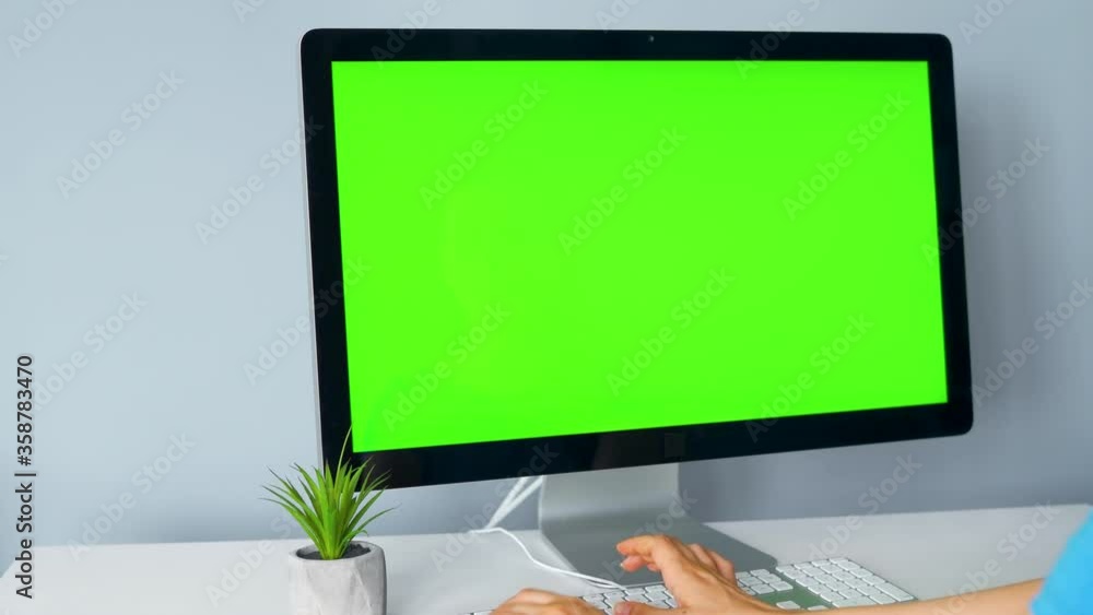 Woman typing on a computer keyboard, monitor with a green screen ...