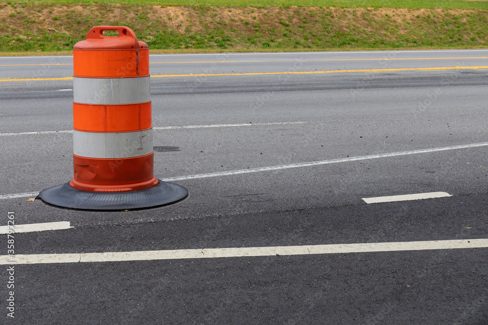 Orange and white striped traffic safety barrel on an asphalt street ...