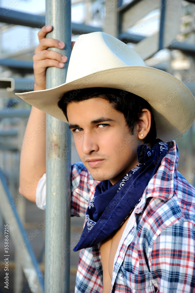 Young masculine and handsome cowboy poses by the bleachers after riding ...