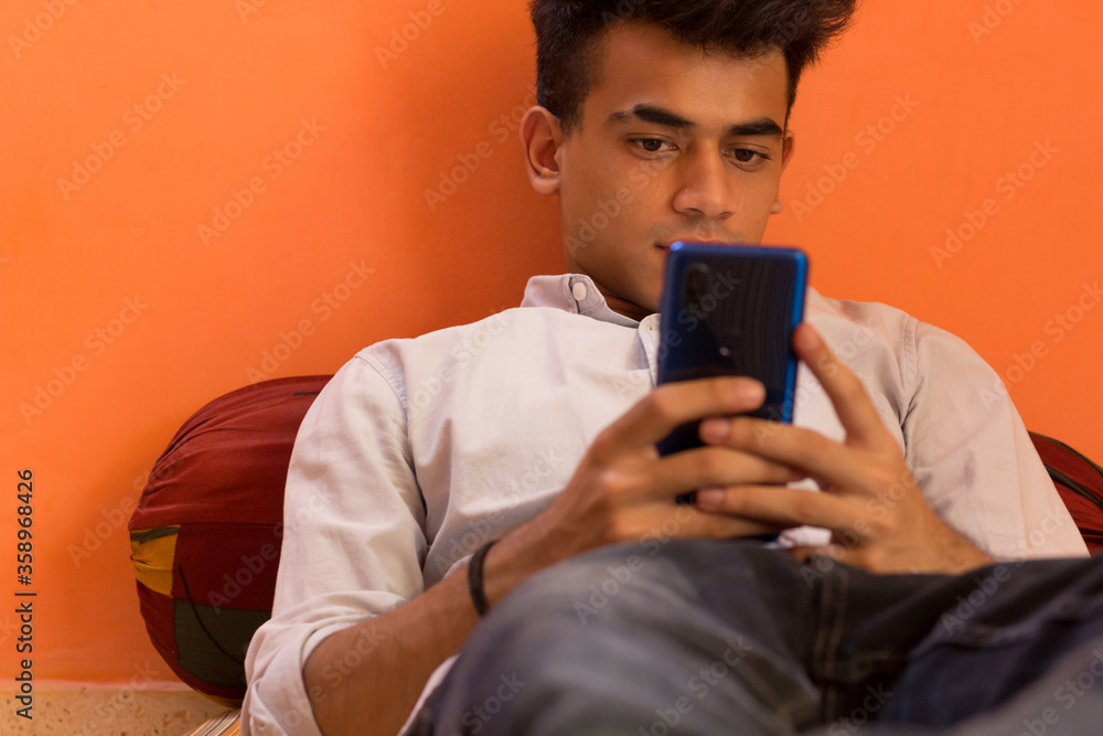 A Young Man looking at his cellphone while lying down over a pillow on ...