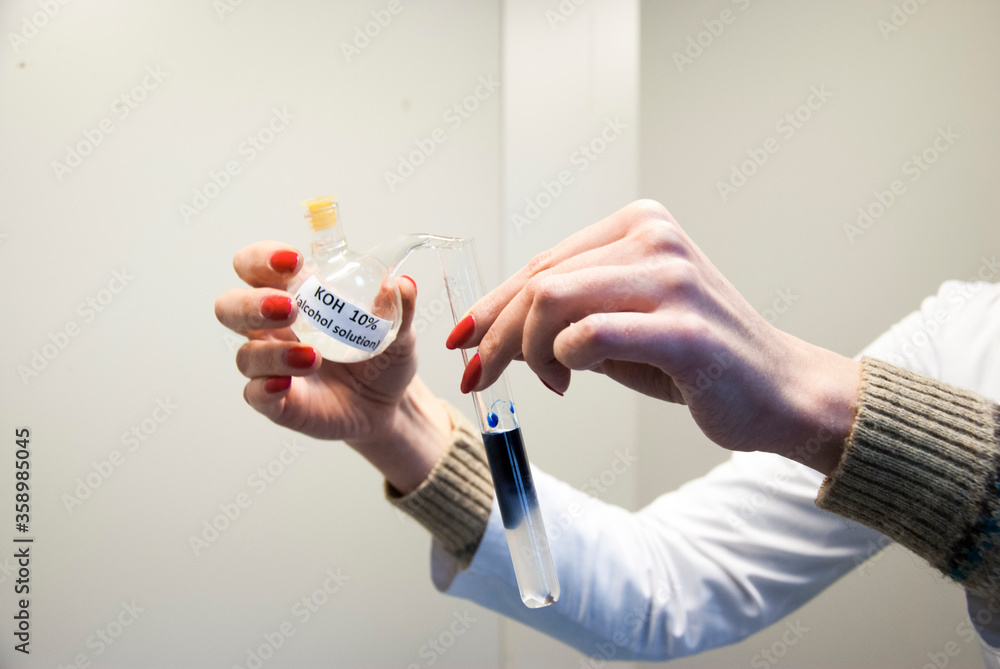 Female laboratory technician putting Potassium Hydroxide (KOH) into ...