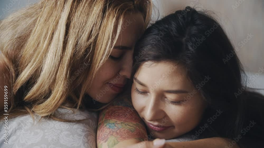 Close portrait of cute multiracial lesbian girls hugging in bed ...