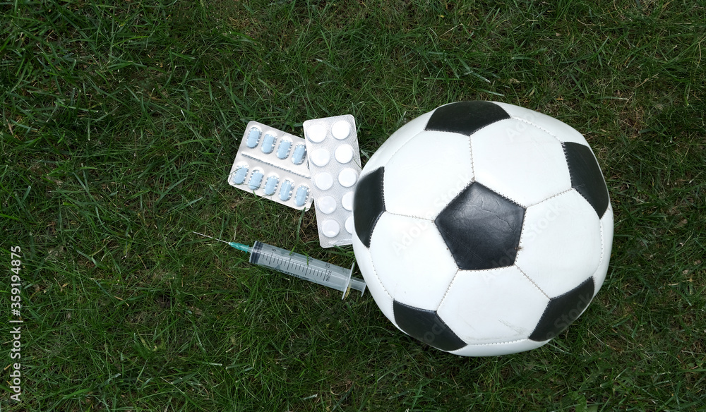 Football, soccer ball near the syringe and pills on the lawn. The ...