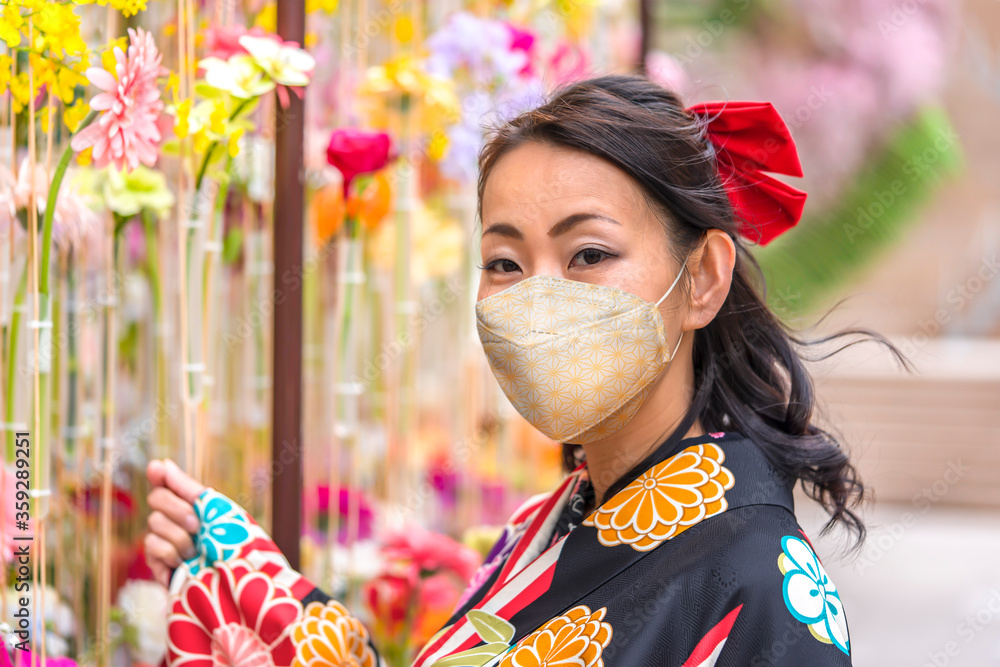 Japanese woman wearing a face mask in hakama kimono in front of a wall ...