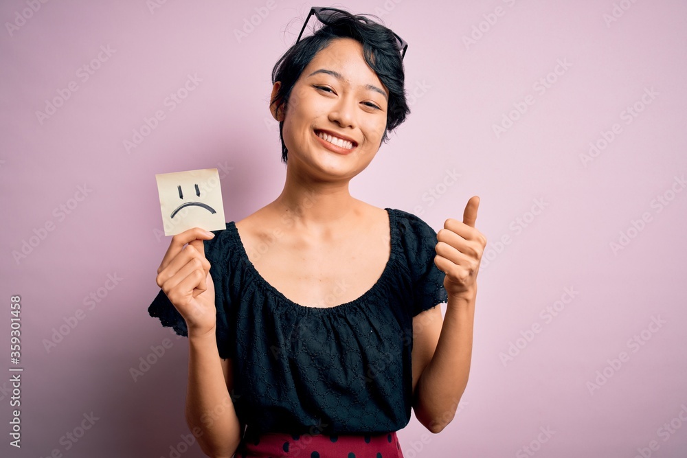 Young beautiful asian girl holding reminder with unhappy face emotion ...