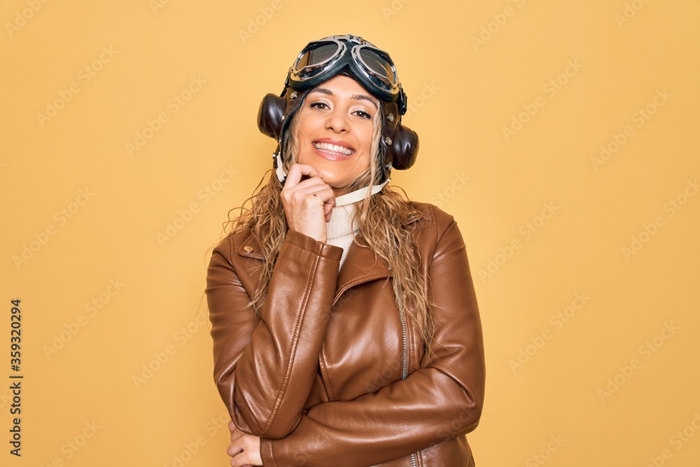 Young beautiful blonde aviator woman wearing vintage pilot helmet whit ...