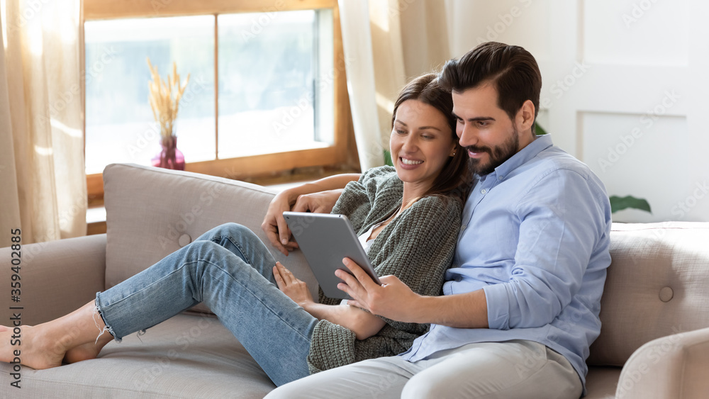 Happy young couple relaxing on cozy couch, using computer tablet ...
